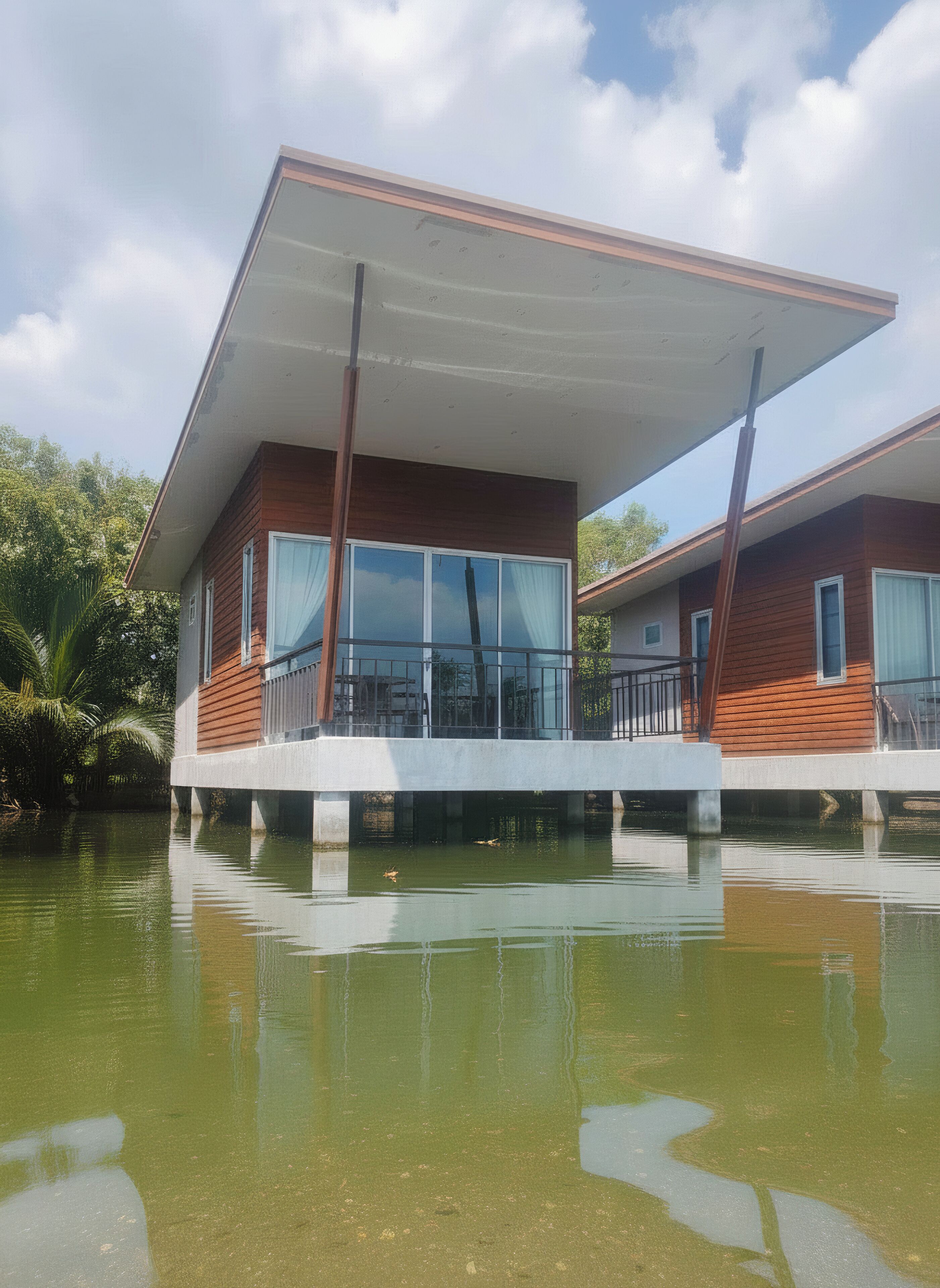 Uma casa moderna com telhado plano, janelas amplas e uma varanda. Localiza-se à beira de um corpo d'água.