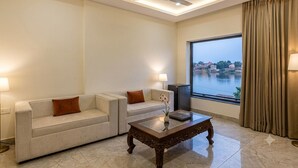 Uma sala de estar moderna com dois sofás, uma mesa de centro, um ventilador de teto e uma grande janela com vista para um corpo de água.