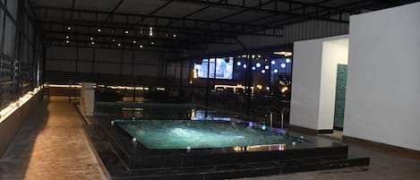 Piscina interior com chão de azulejos, rodeada por paredes e teto alto.