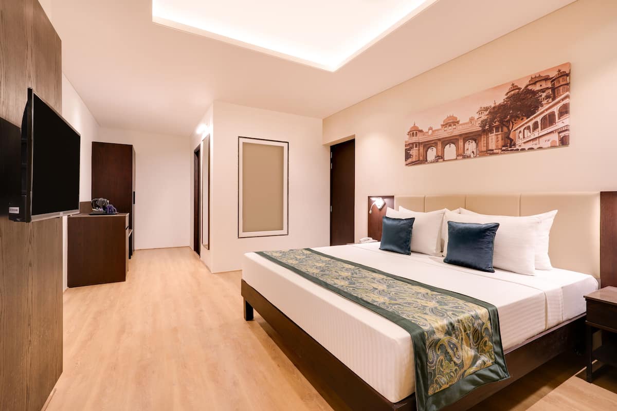 Quarto de hotel com uma cama grande, televisão de tela plana, guarda-roupa de madeira e um quadro na parede.