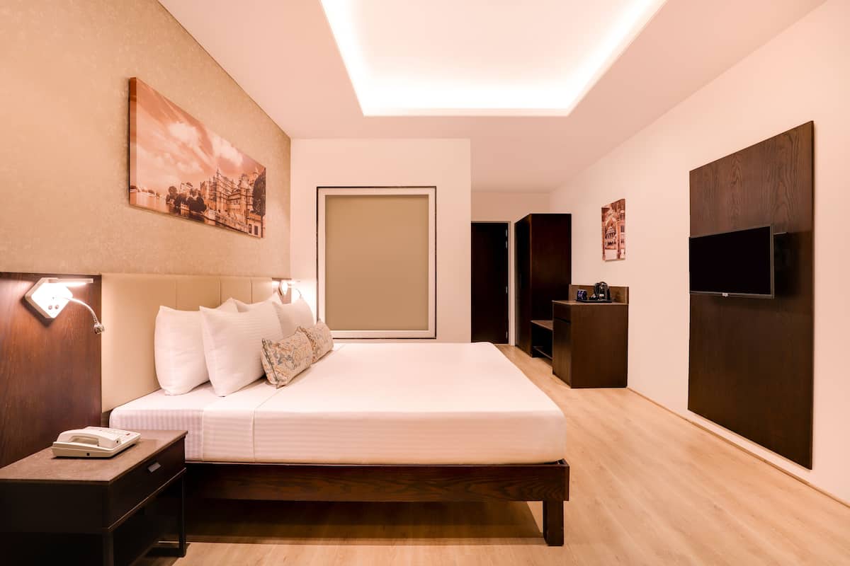Quarto de hotel moderno com uma cama grande, mesas de cabeceira, televisão de tela plana e obras de arte nas paredes.