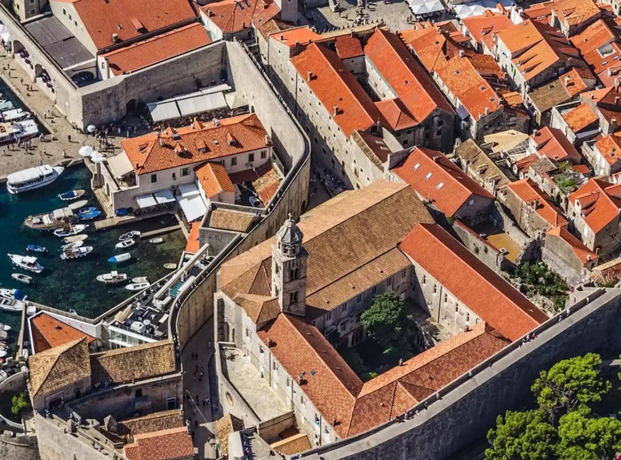 Vista aérea de uma cidade histórica com ruas estreitas, telhados de terracota e uma muralha fortificada.