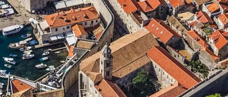 Vista aérea de uma cidade histórica com ruas estreitas, telhados de terracota e uma muralha fortificada.