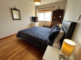 Quarto com uma cama, televisão, penteadeira e janela.