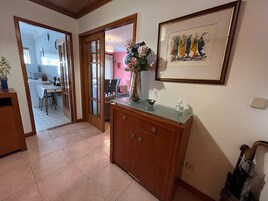 Um corredor com um armário de madeira, uma obra de arte emoldurada e um vaso com flores.