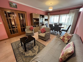 Uma sala de estar com sofá, duas poltronas, mesa de centro e área de jantar com cadeiras e mesa.