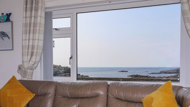 Um sofá de couro marrom com almofadas amarelas, um quadro na parede e vista para o mar pela janela.