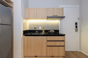 Cozinha compacta com armários de madeira, bancada preta e coifa de aço inoxidável.