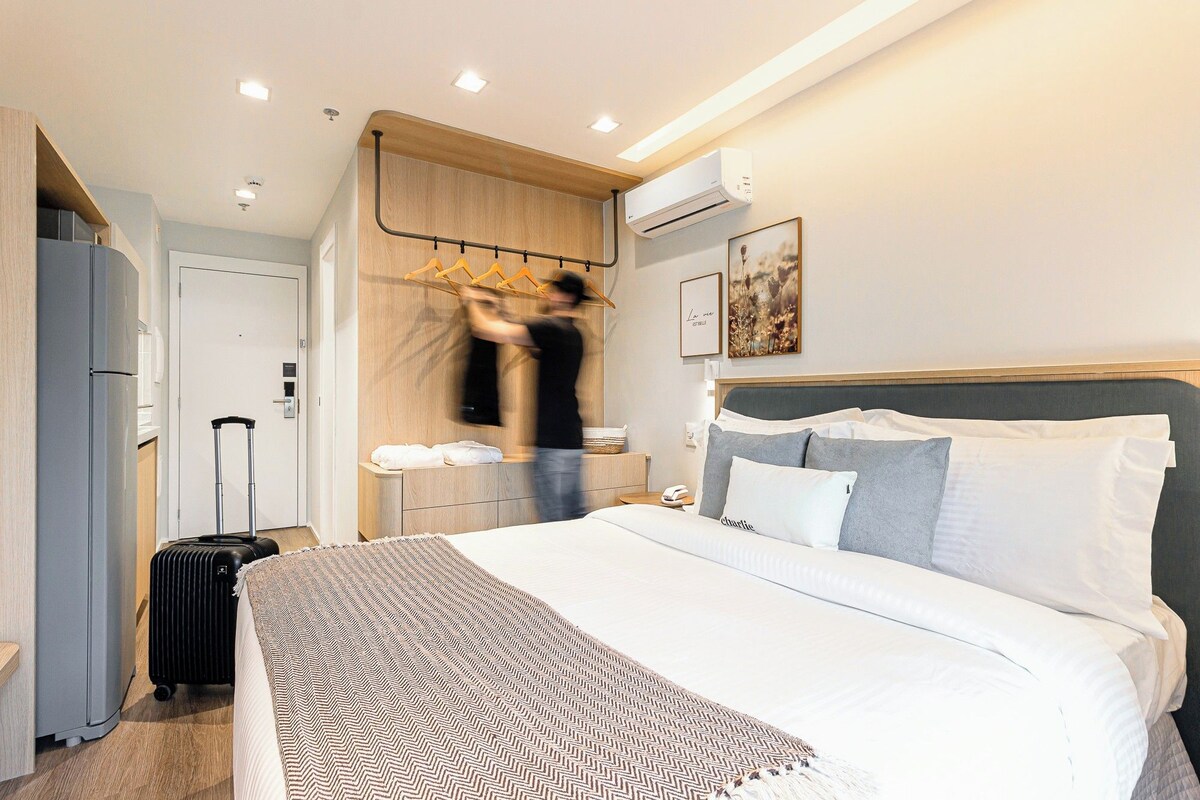 Quarto de hotel com uma cama, um guarda-roupa, uma mala e um ar condicionado fixado na parede.