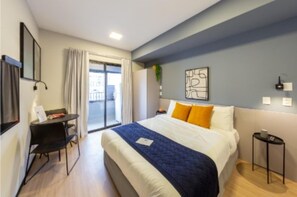 Quarto de hotel moderno com uma cama grande, uma escrivaninha e vista para o exterior.