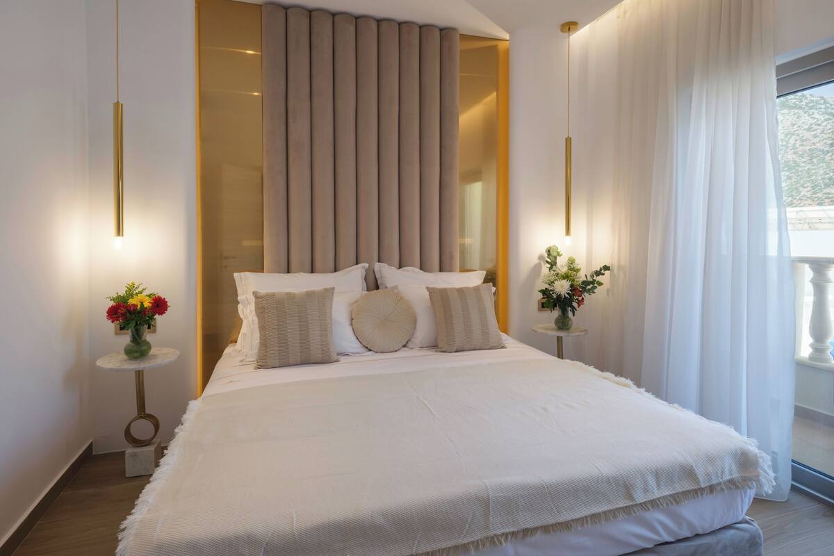 Quarto moderno com uma cama grande, duas mesas de cabeceira e vista para o exterior.