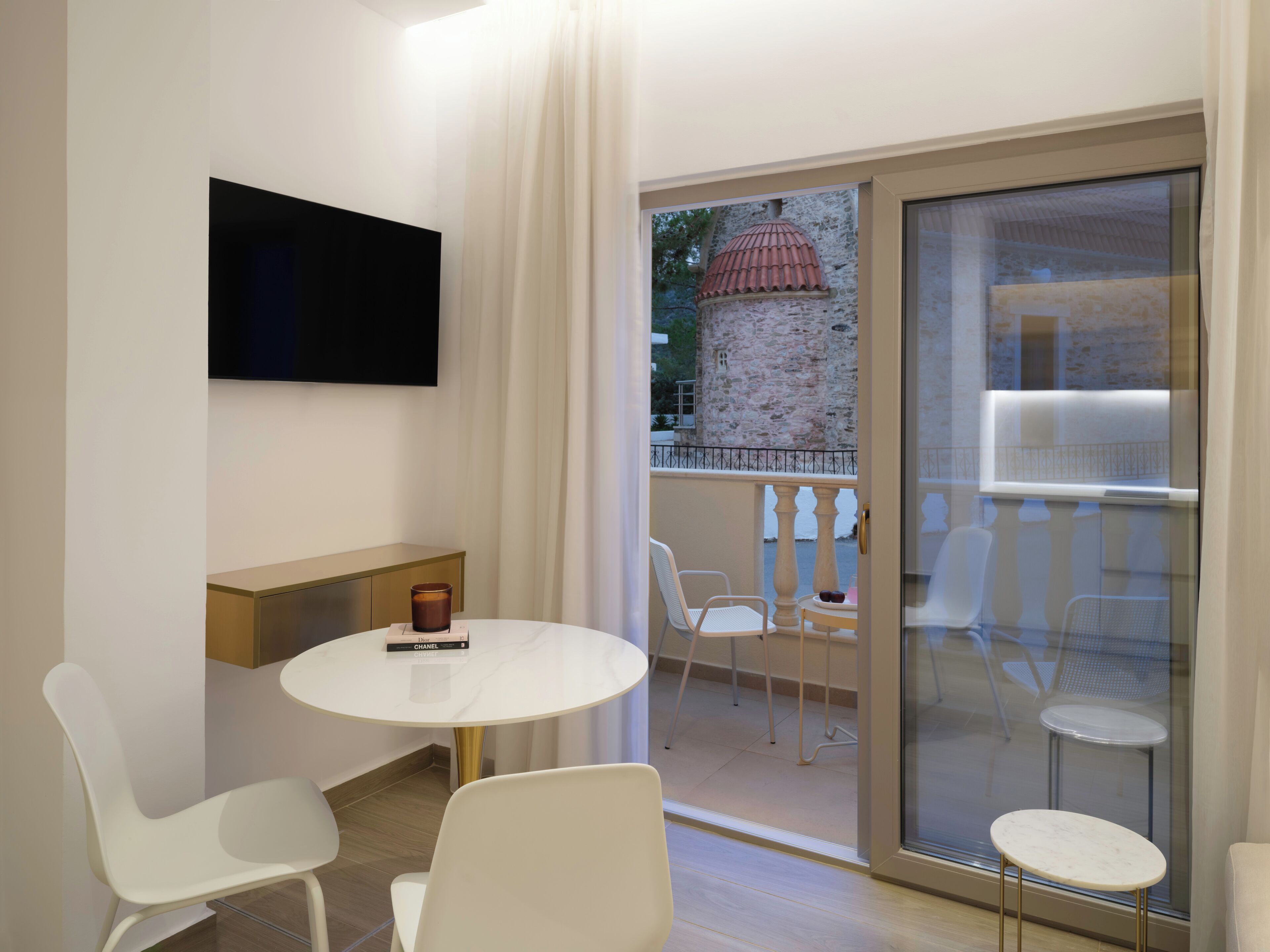 Quarto de hotel moderno com varanda, televisão de tela plana, mesa redonda com cadeiras e uma pequena mesa redonda com uma cadeira.