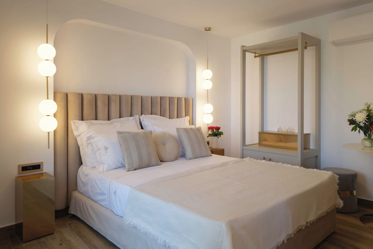 Um quarto moderno com uma cama grande, mesas de cabeceira, um espelho e um candeeiro fixado na parede.
