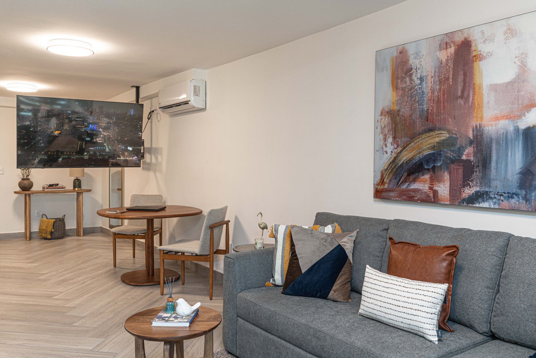 Uma sala de estar com um sofá cinzento, uma mesa de centro, uma televisão e um quadro na parede.