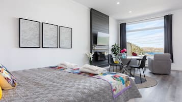 Quarto de hotel moderno com uma cama grande, uma escrivaninha com cadeira, uma televisão e vista para o mar.