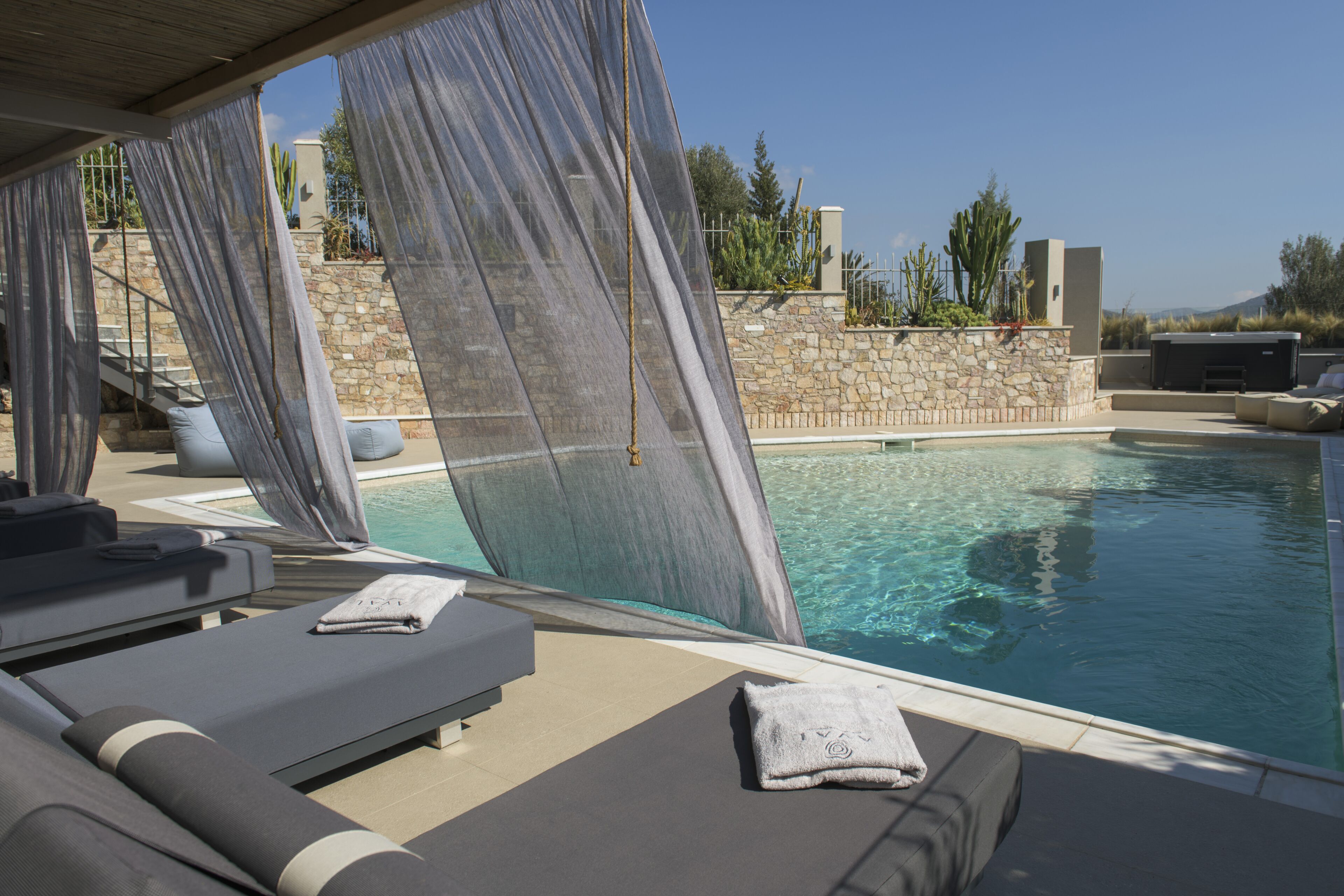 Uma área à beira da piscina com espreguiçadeiras, um muro de pedra e vista para a piscina.