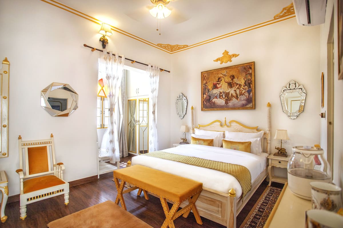Um quarto com uma cama grande, um banco, um espelho e um quadro na parede.
