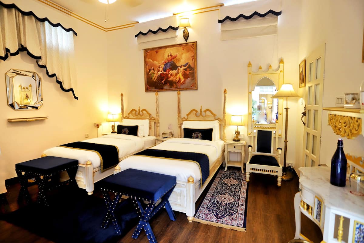 Quarto de hotel com duas camas, uma mesa de cabeceira, uma cadeira, uma mesa e um quadro na parede.