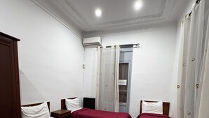 Quarto de hotel com três camas, piso estampado e teto com molduras decorativas.