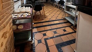 Interior de restaurante com parede de pedra, chão em azulejo e área de buffet com pratos empilhados.