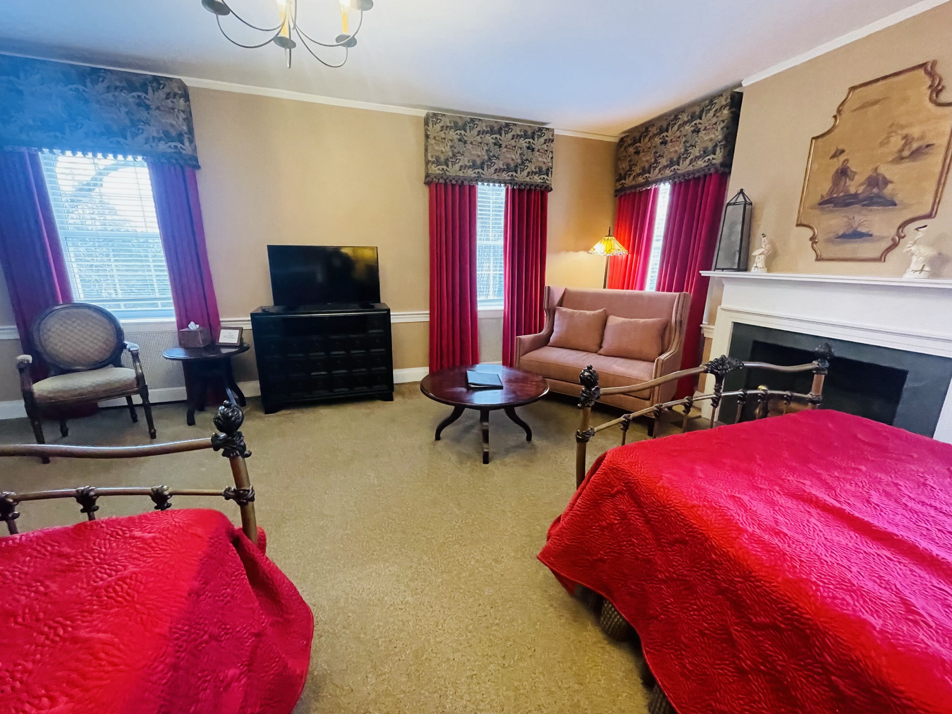 Quarto de hotel com cama, sofá, televisão, lareira e lustre.