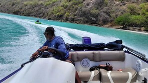 Um barco com uma pessoa a leme, rodeado por águas azul-turquesa e uma costa rochosa.