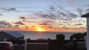 Pôr do sol sobre o oceano, com vista para uma área costeira, incluindo um edifício e um portão.