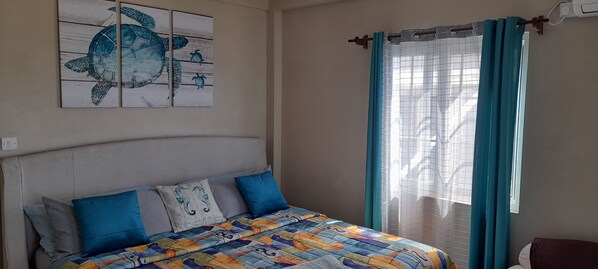 Quarto com cama, cabeceira, uma obra de arte de tartaruga na parede e janela com cortinas.