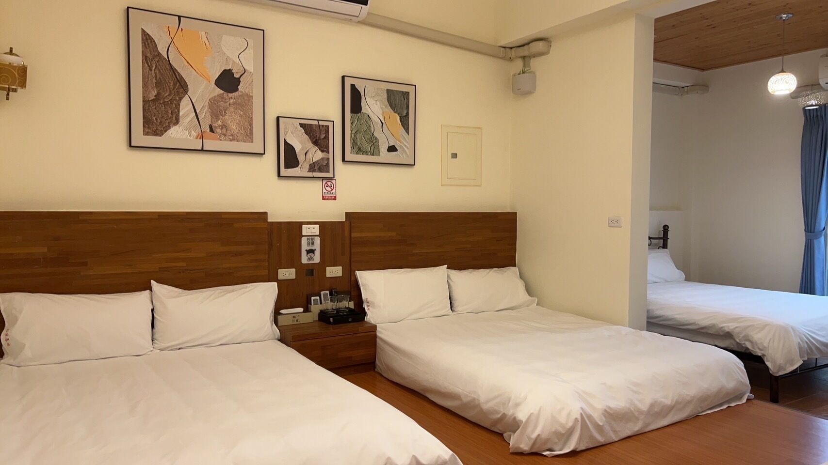 Quarto de hotel com duas camas, cabeceiras de madeira, roupa de cama branca e obras de arte abstratas nas paredes.