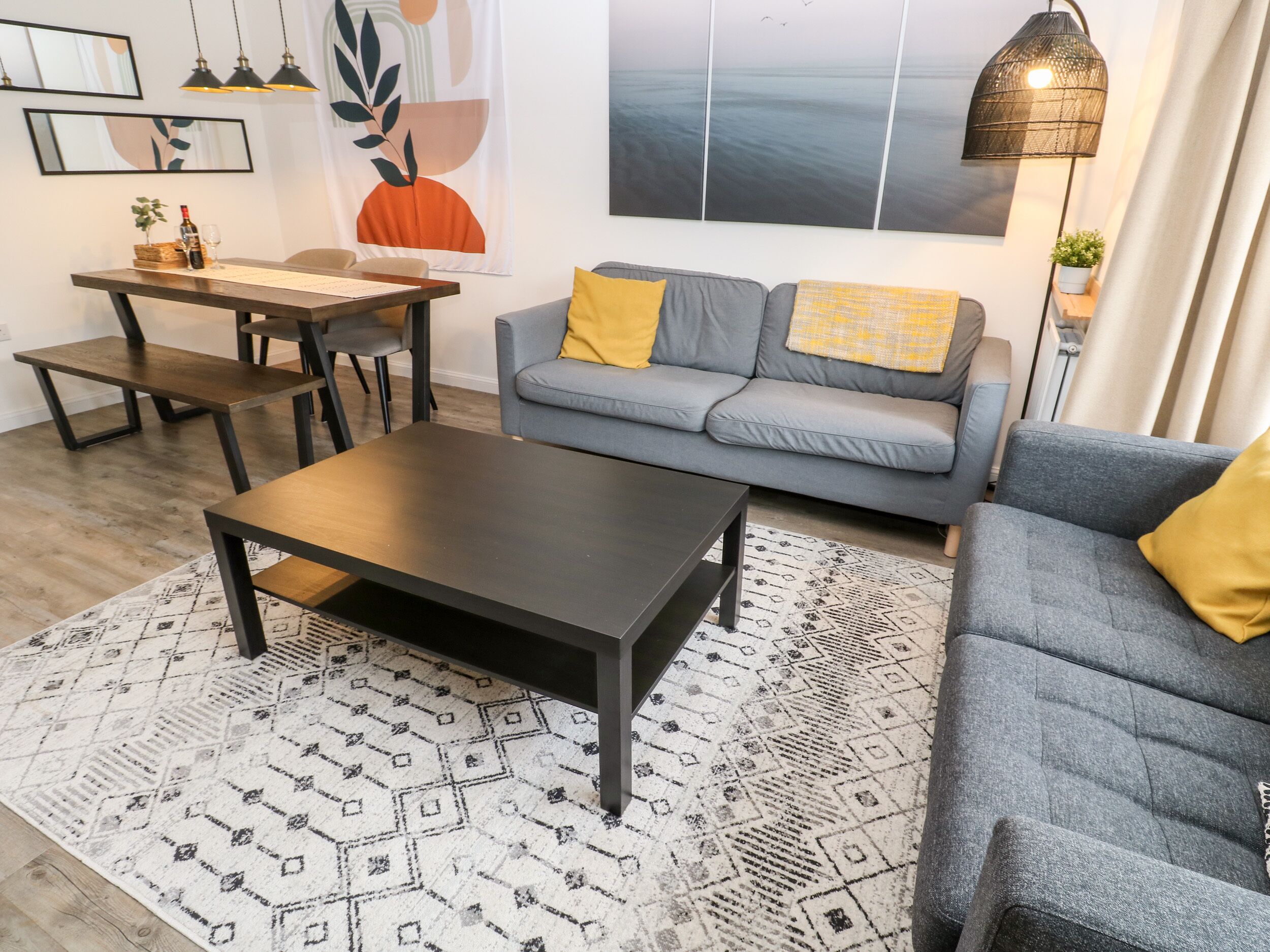 Uma sala de estar moderna com um sofá cinzento, uma mesa de centro, uma mesa de jantar com cadeiras e um tapete estampado.