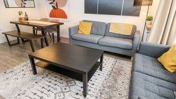 Uma sala de estar moderna com um sofá cinzento, uma mesa de centro, uma mesa de jantar com cadeiras e um tapete estampado.