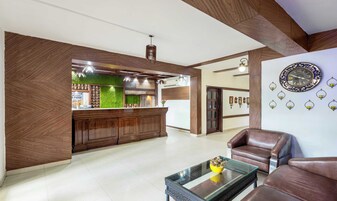 Um hall amplo com balcão de atendimento em madeira, uma parede verde e um relógio na parede.