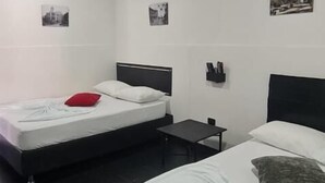 Quarto de hotel com duas camas, uma mesinha e um ventilador de teto.