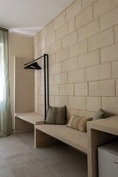 Quarto moderno com parede de tijolos bege, um banco com almofadas, um cabideiro suspenso e um pequeno armário.