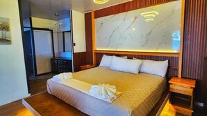 Quarto moderno com cama grande, piso de madeira, parede de mármore e luminária no teto.