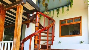 Uma escada espiral de madeira leva a um andar superior, uma janela grande com vista para o exterior e uma área de estar com sofá e uma mesinha.