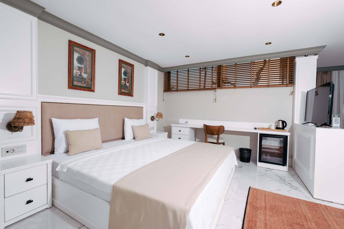 Quarto de hotel moderno com uma cama grande, uma escrivaninha, uma cadeira, um refrigerador pequeno e uma TV.