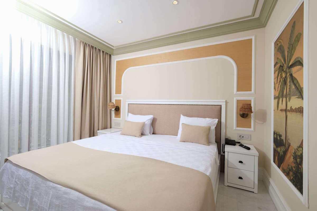 Quarto de hotel com uma cama grande, uma mesinha de cabeceira, uma luminária e um quadro na parede.