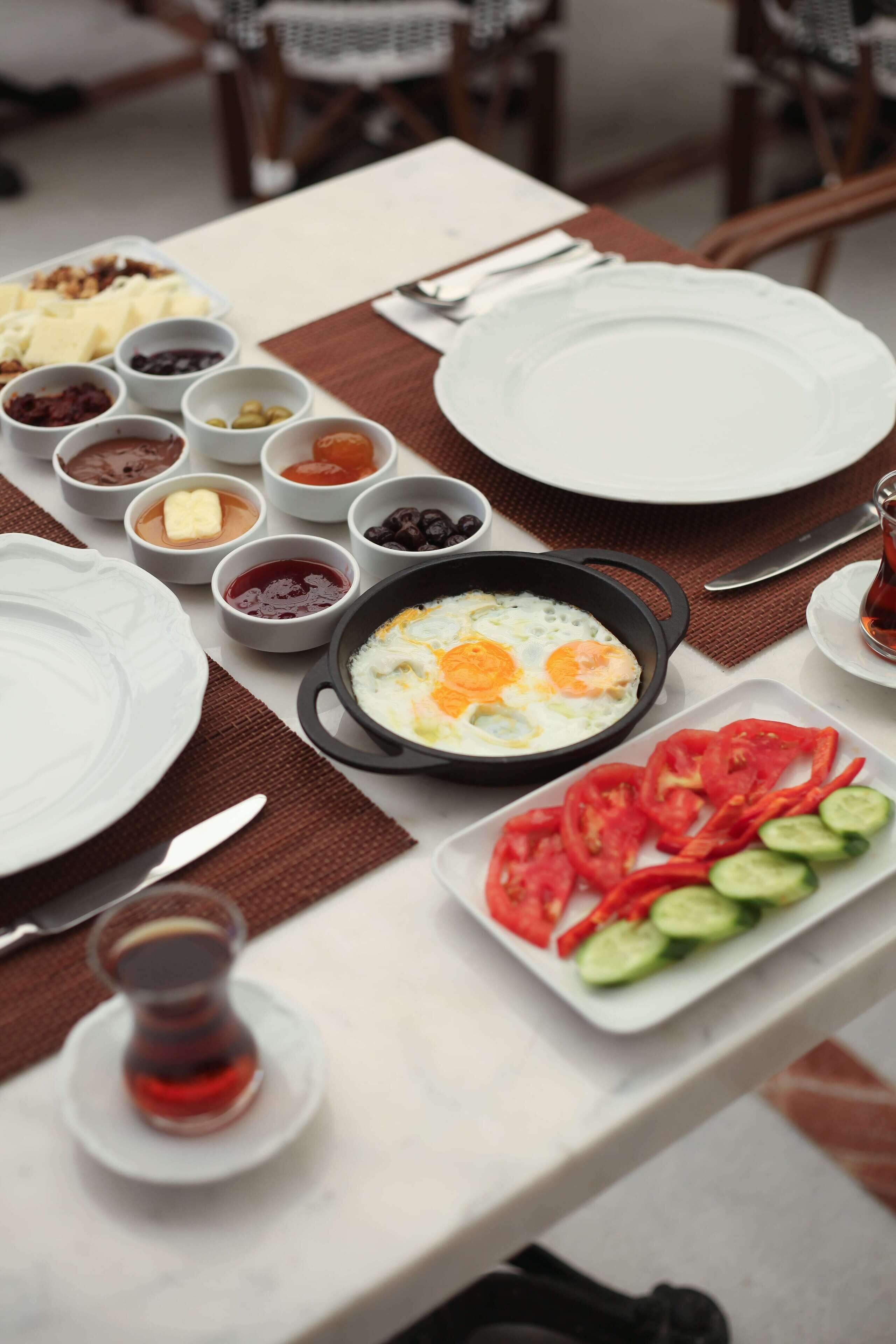 Mesa posta com diversos pratos, incluindo ovos, tomates, pepinos e acompanhamentos.