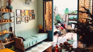 Uma sala de estar acolhedora com um sofá, uma mesa de centro e uma estante de livros. Há uma janela grande com vista para o exterior.