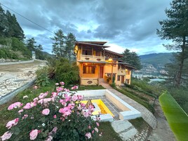 Uma casa de dois andares com varanda, cercada por vegetação e vista para o vale.