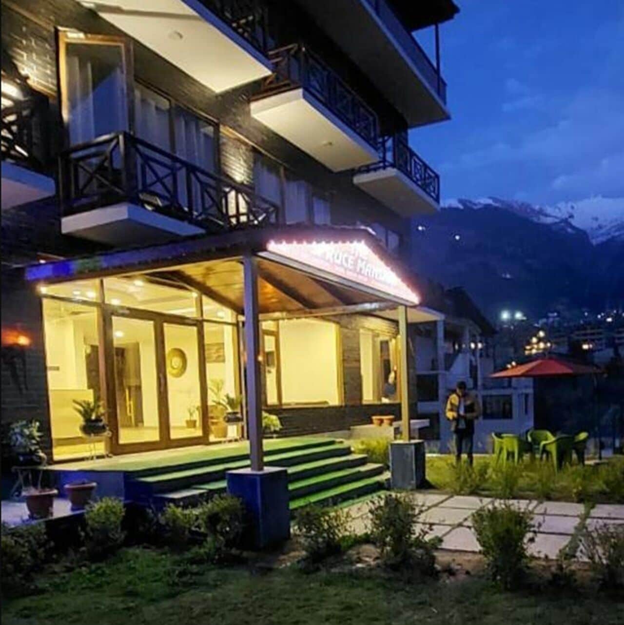 Um hotel com fachada de vidro, área de estar ao ar livre e montanhas ao fundo.