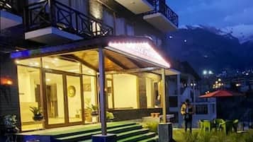 Um hotel com fachada de vidro, área de estar ao ar livre e montanhas ao fundo.