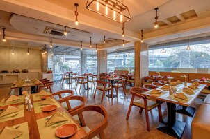Restaurante com várias mesas preparadas para refeições, cadeiras de madeira e decoração de interiores moderna.