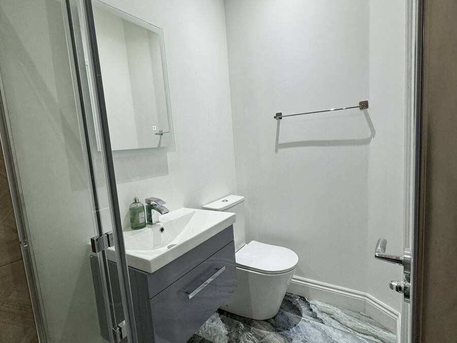 Uma casa de banho moderna com chuveiro em cabine de vidro, lavatório branco e sanita.
