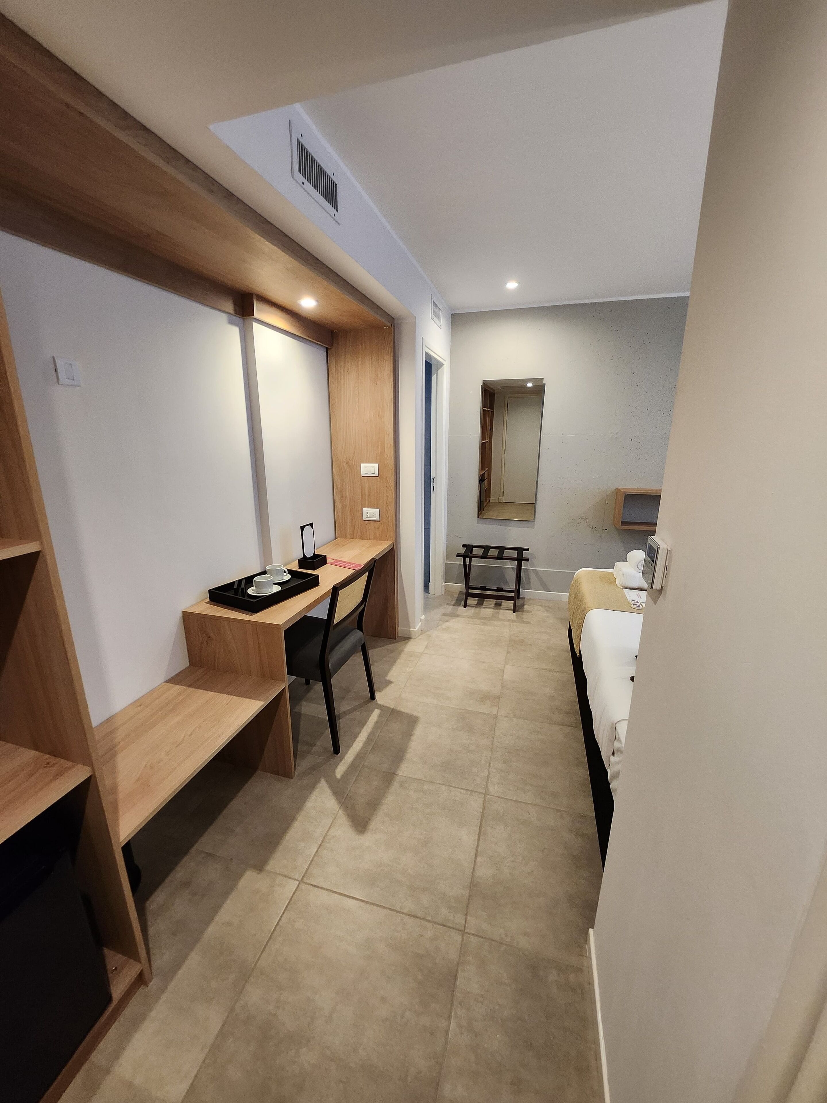Quarto de hotel compacto com uma escrivaninha de madeira, uma cama, uma mesinha e um espelho.
