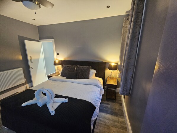 Quarto de hotel com cama, luminárias de cabeceira, radiador e porta.