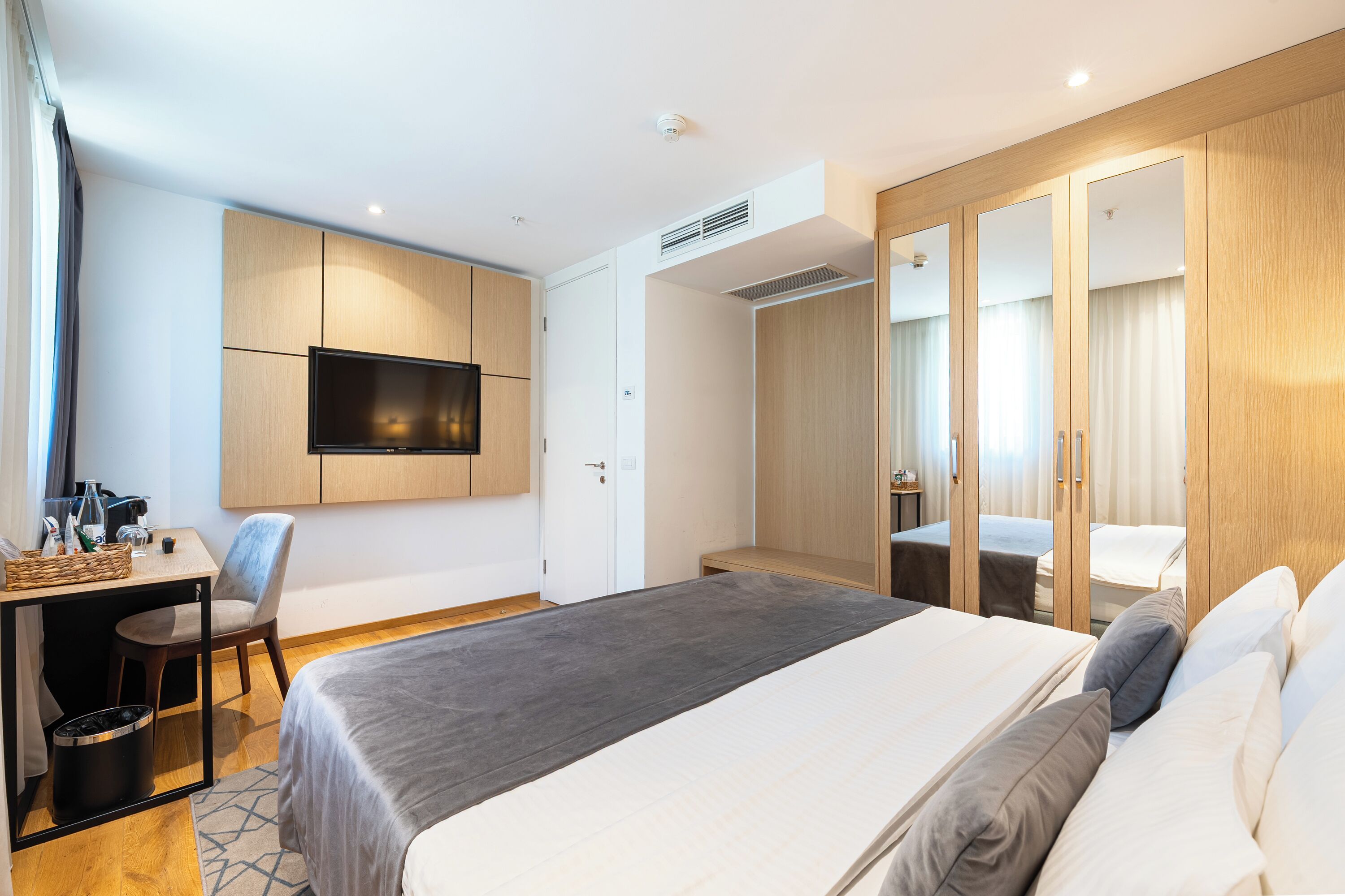 Quarto de hotel com cama, escrivaninha, cadeira, televisão e guarda-roupa.