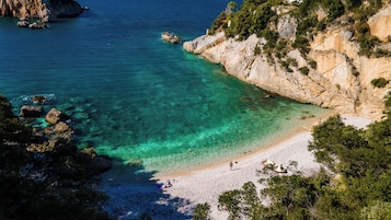 Uma praia costeira com águas turquesa cristalinas, afloramentos rochosos e uma faixa de areia.