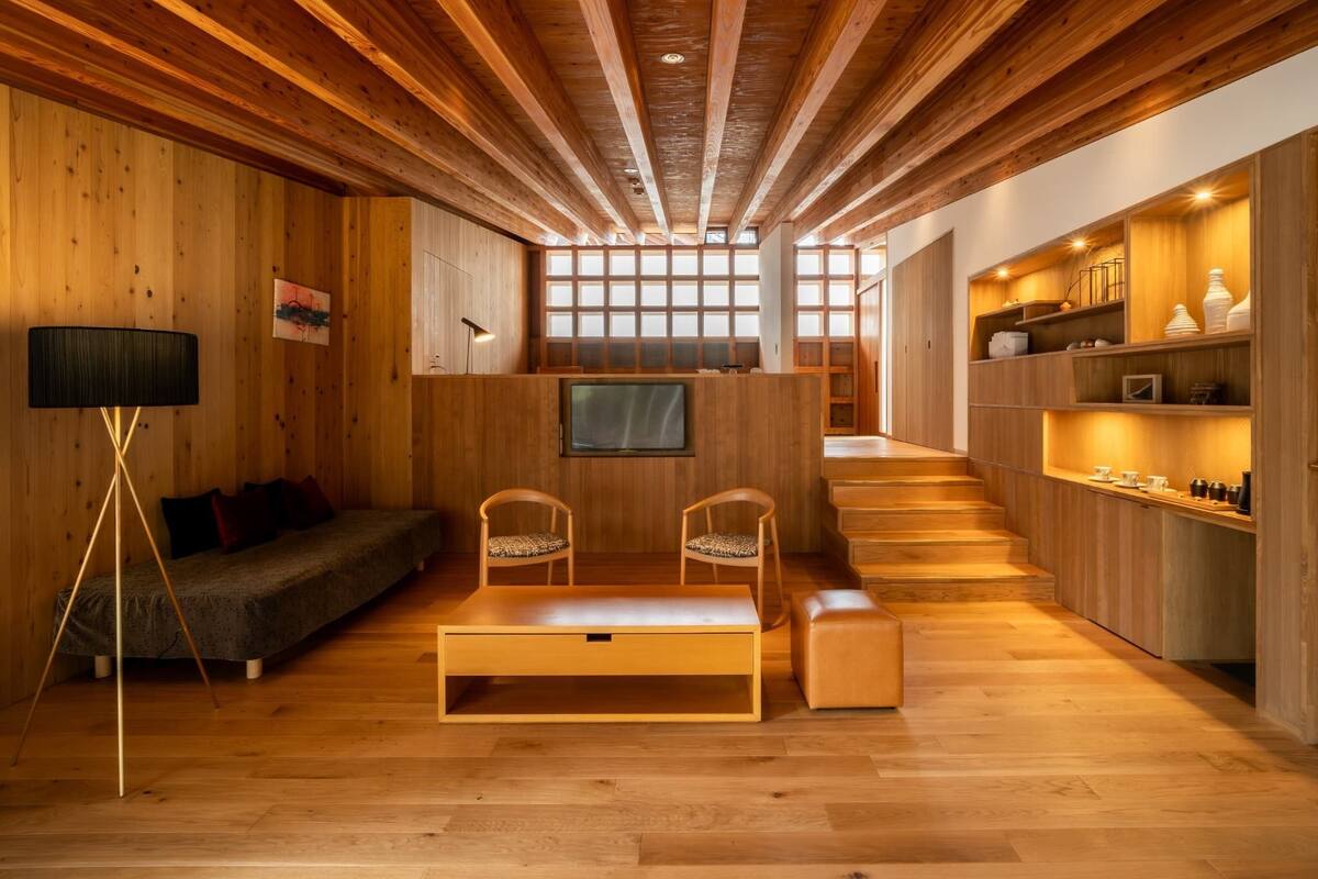 Um interior em madeira com um sofá, duas cadeiras, uma TV e um banco de madeira.